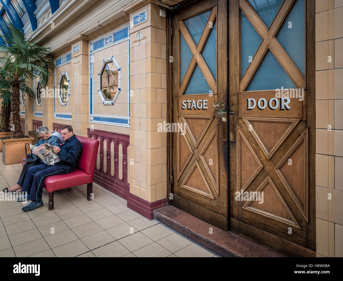 Couple sat on seat reading paper next to Stage Door in the Floral Hall ...