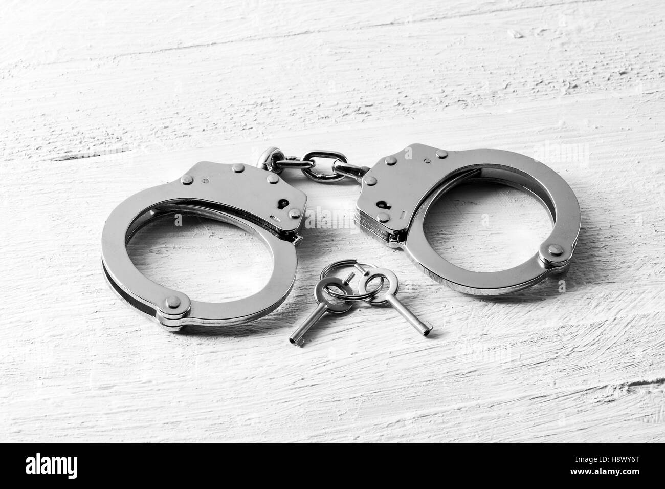 Locked pair of steel handcuffs lying on a textured white board with the ...