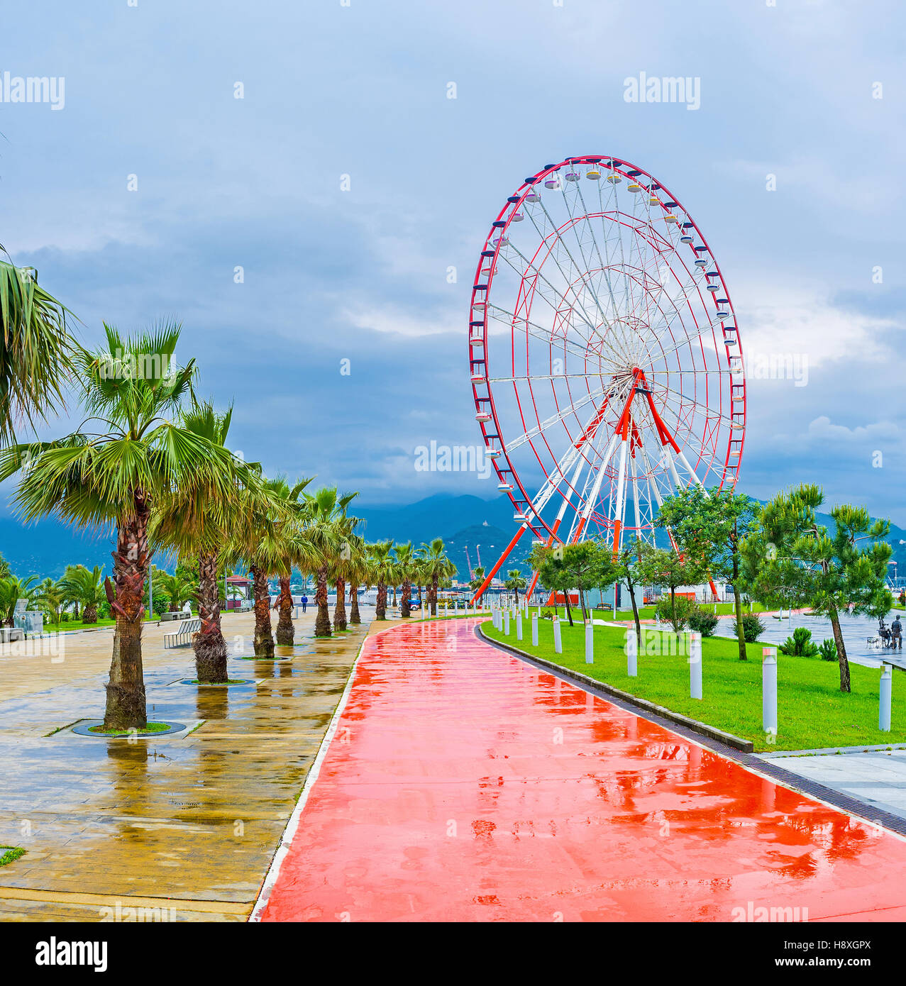 The wet road of the Miracle Park with the ferris wheel and the foggy ...