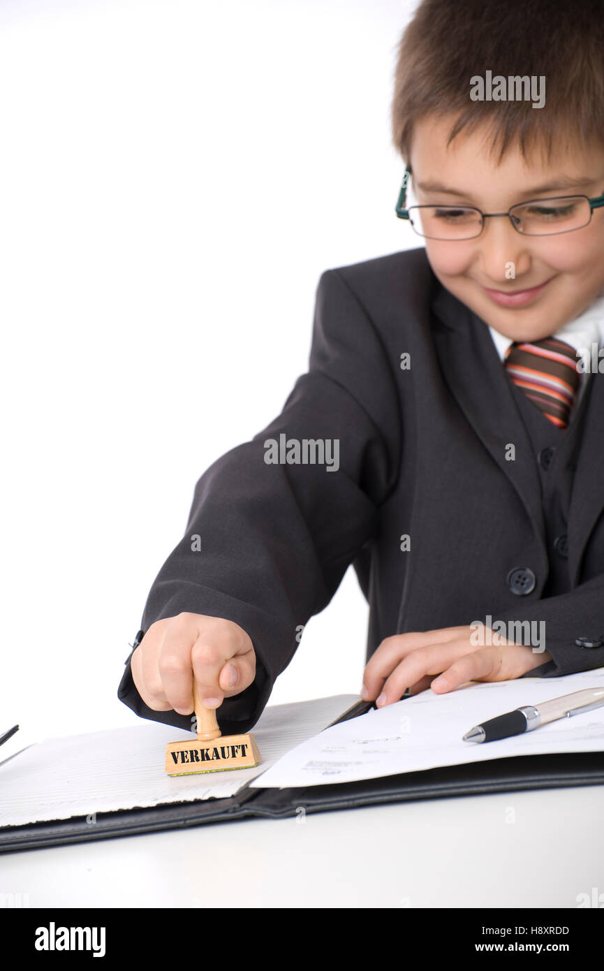Boy dressed as a businessman stamping with a SOLD stamp in an office ...