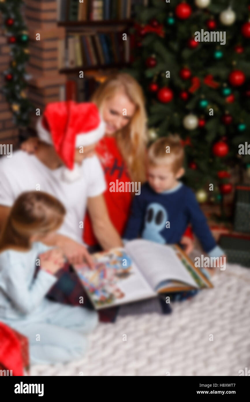 Dad reading book to his family at Christmas tree Stock Photo - Alamy