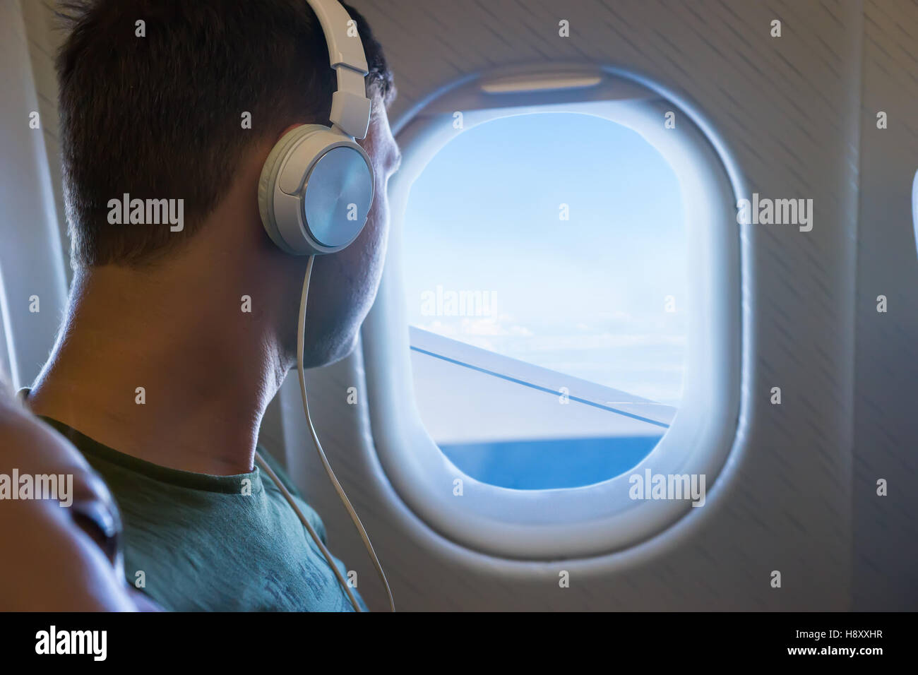 Young man listening music with headphones and looking out the window of ...