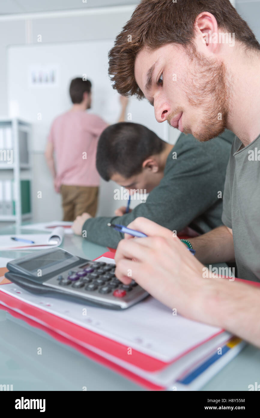 teenage schoolboy using calculator while studying at desk in classroom ...