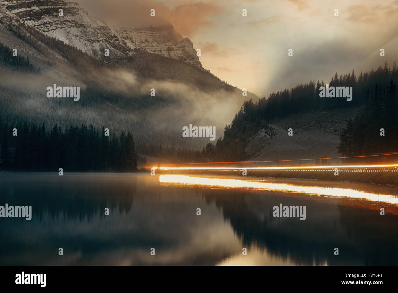 Mountain lake and traffic light trail with reflection and fog at sunset ...