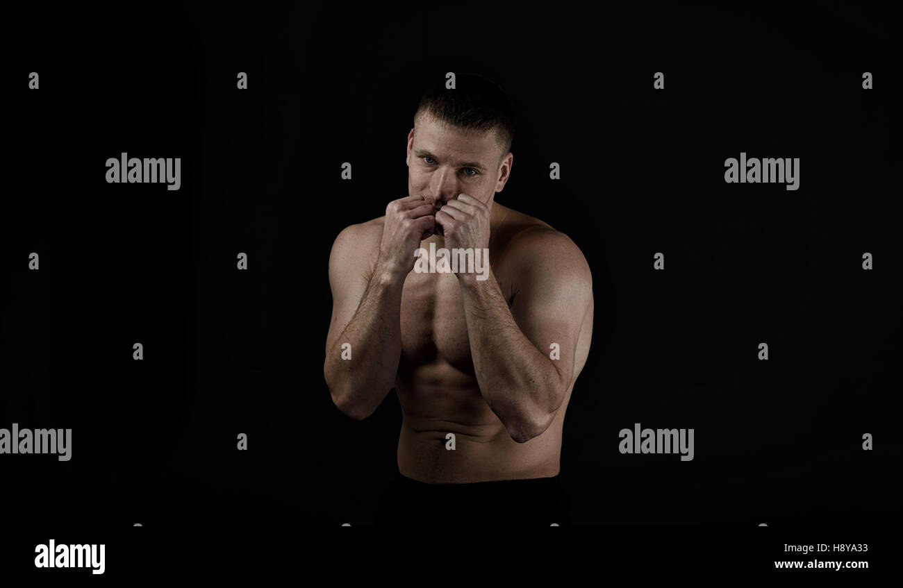Young muscular man with boxing defensive stance against a black ...