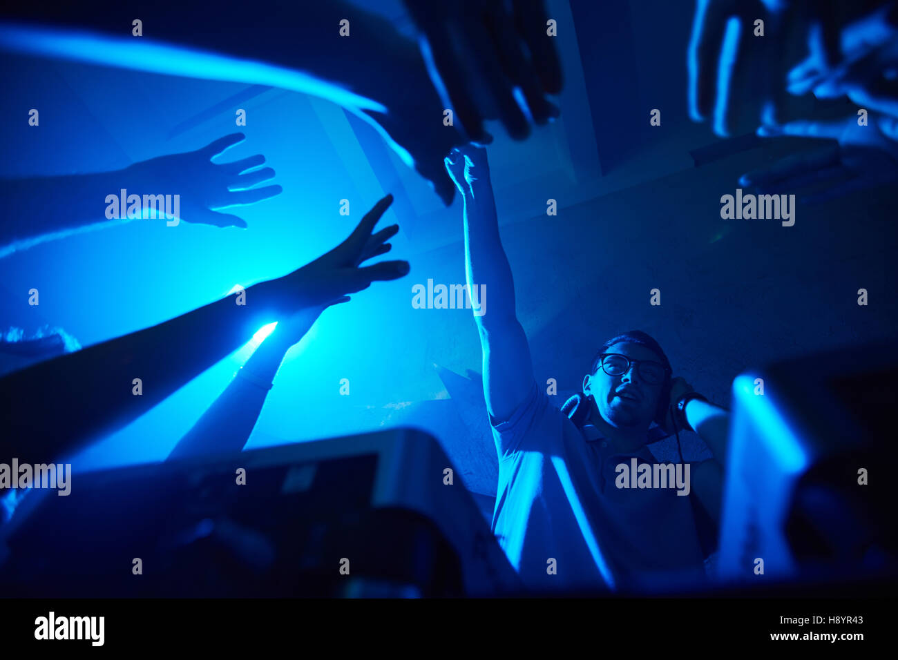 Young deejay with headphones and hands of dancers in night club Stock ...