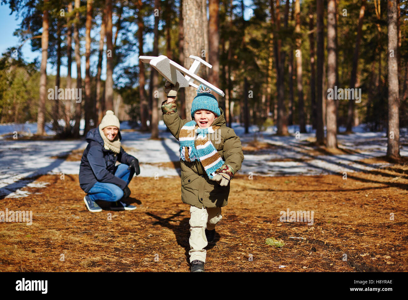 Ecstatic boy running down dry forest ground while launching toy plane ...