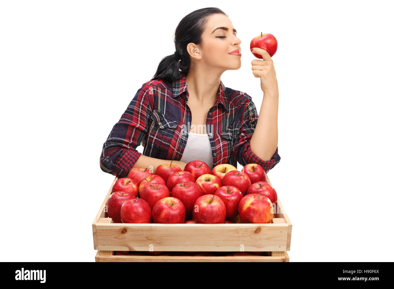 Female farmer smelling an apple behind a crate filled with apples ...