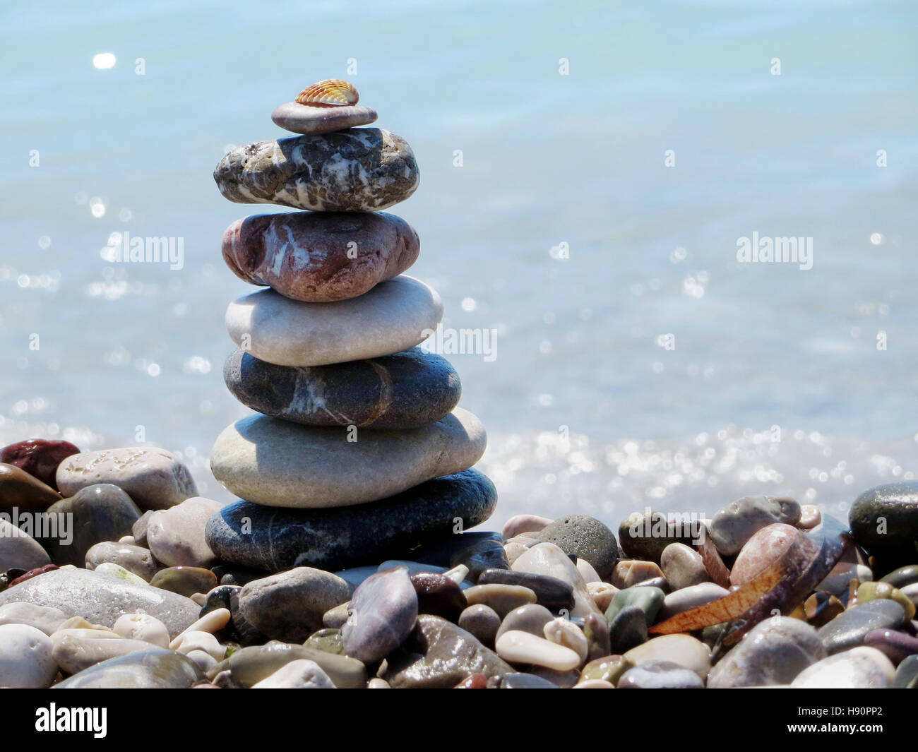 Pyramid of large pebbles with shell on top on the beach. The sea is the ...