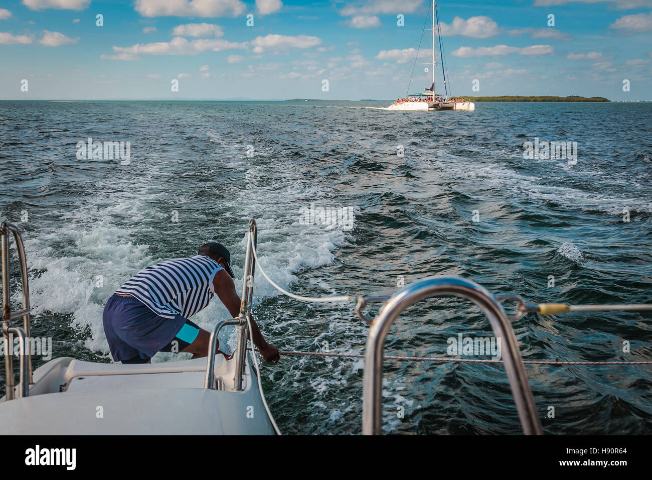 Steersman busy at the rear of catamaran, with another catamaran ...