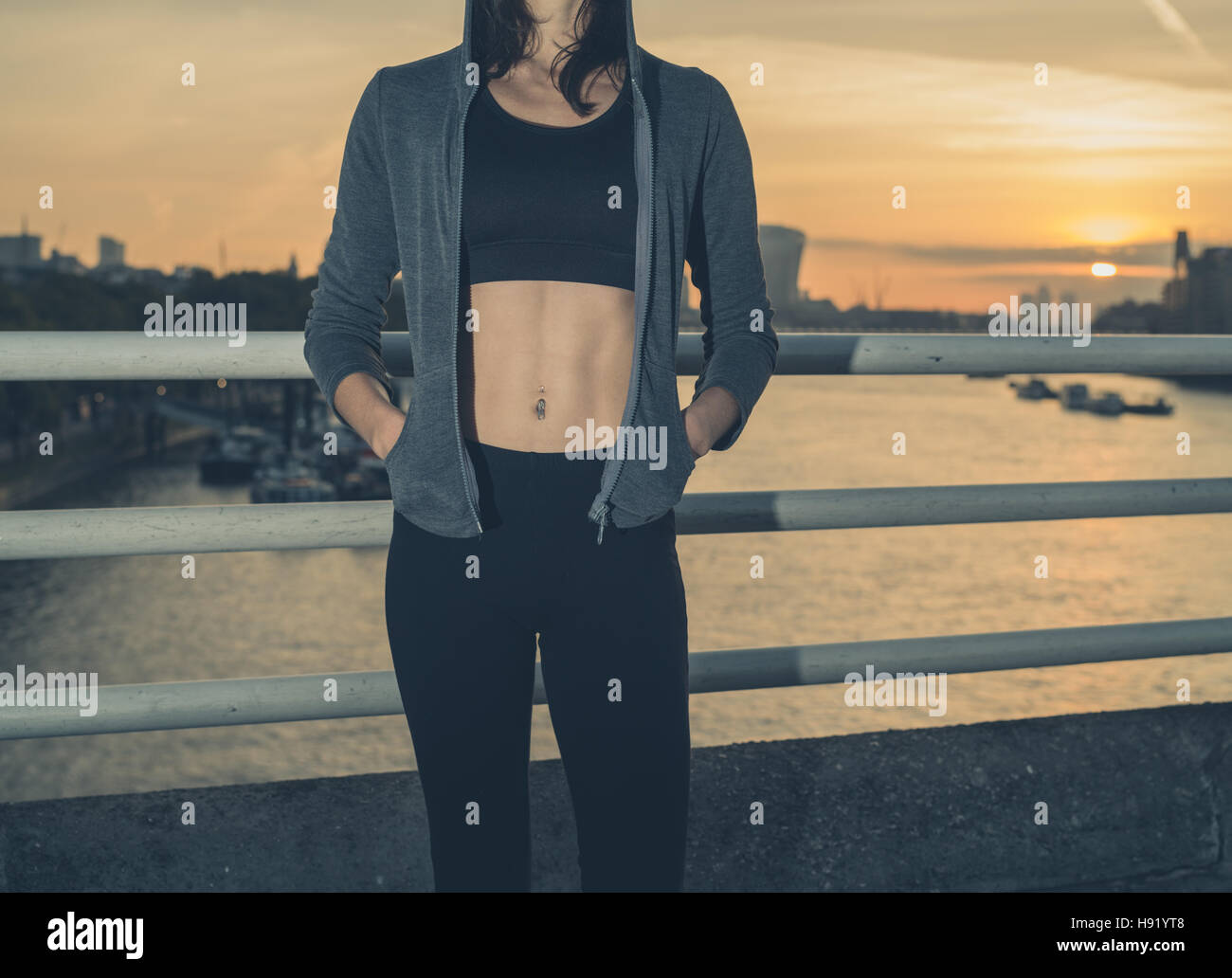 An athletic young woman with toned abs is standing on a bridge in ...