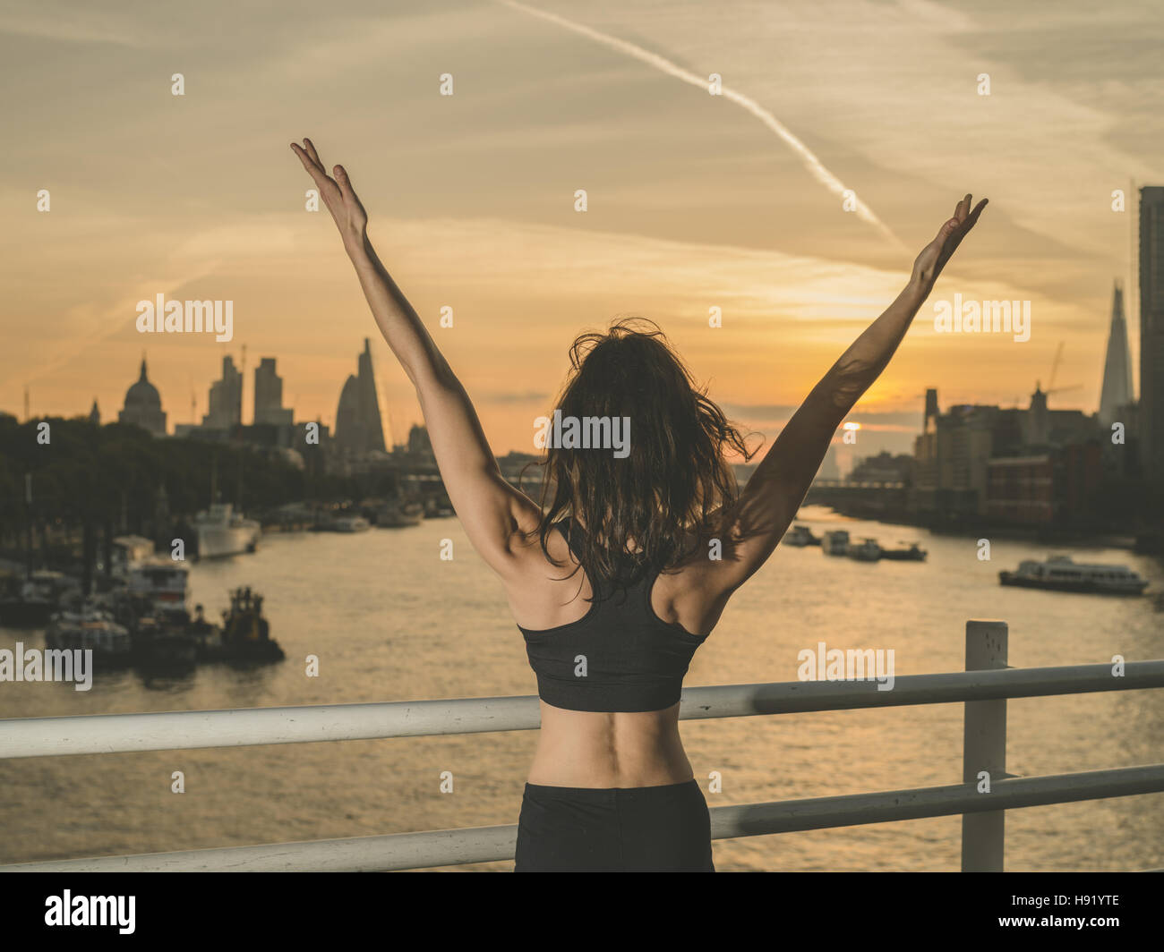 An athletic young woman wearing a sports bra is raising her arms in joy ...