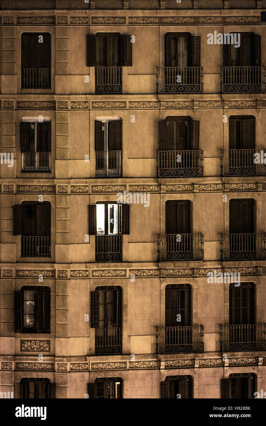 A single apartment light shines through the dark facade of a downtown ...