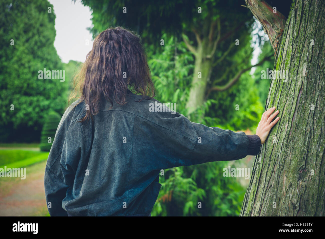 A young woman is leaning and resting her hand on a tree in a country ...