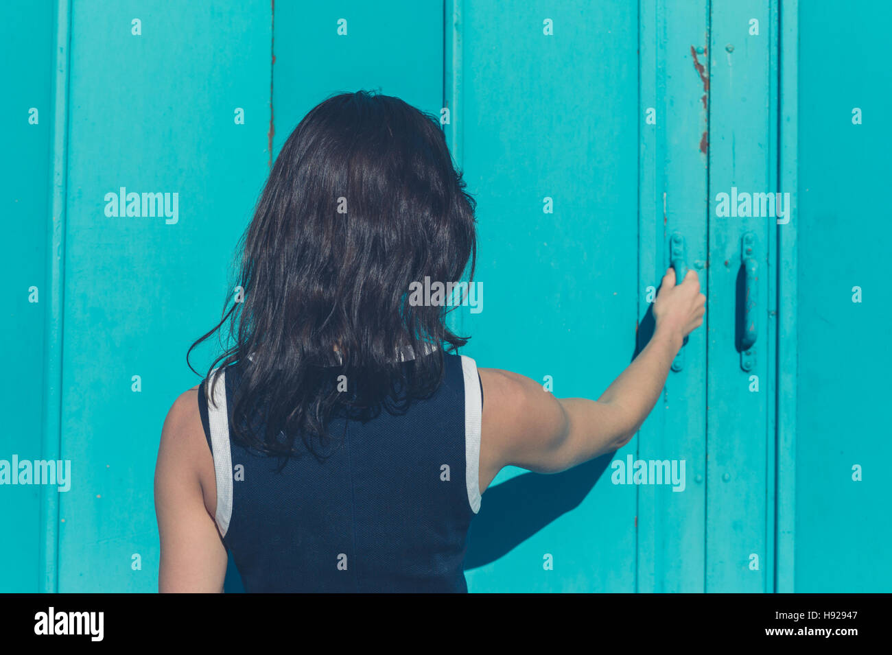 A young woman is grabbing the handle of a blue door outside Stock Photo ...