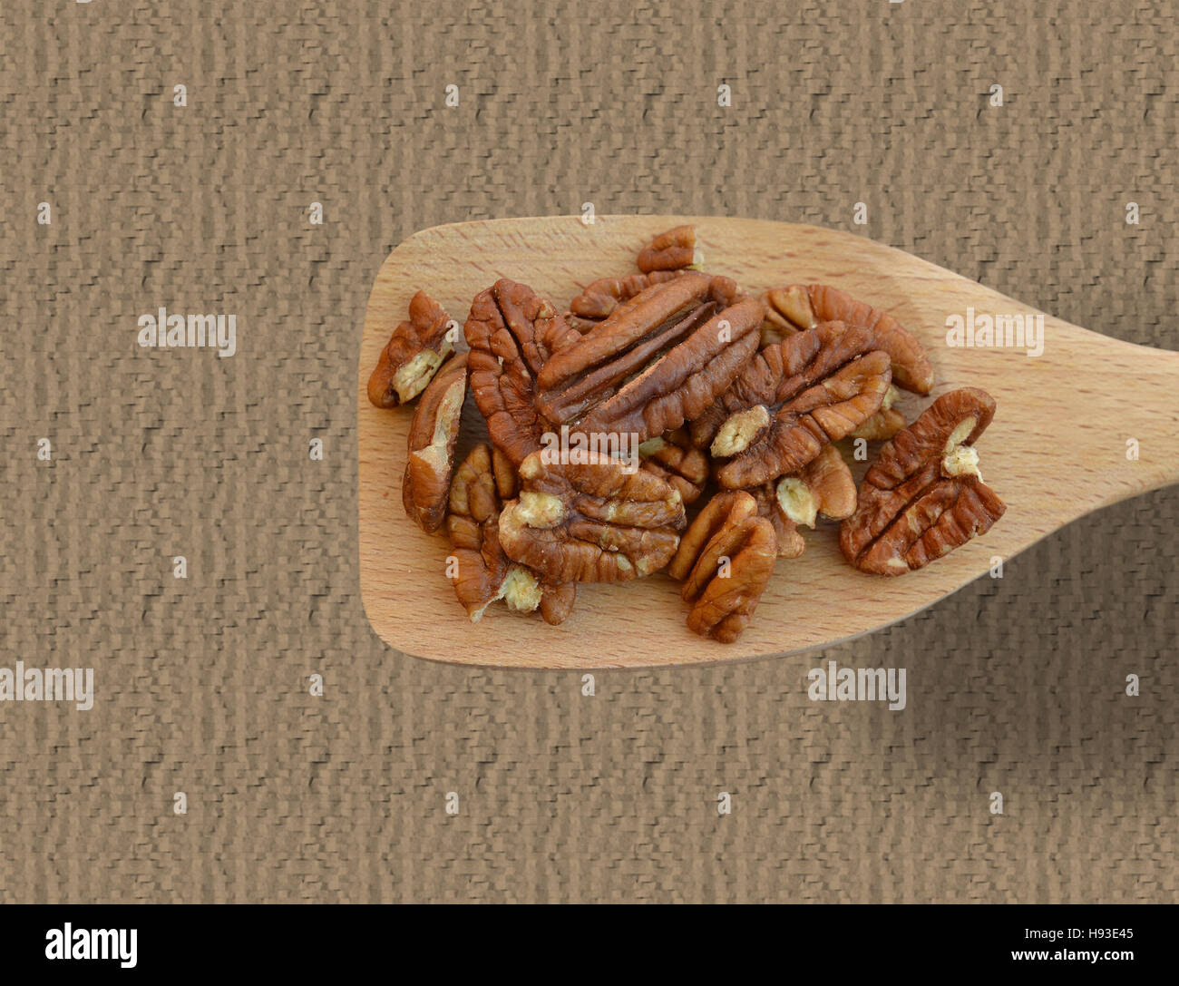 Wide rectangular wooden spoon filled with pecan halves, against tan ...