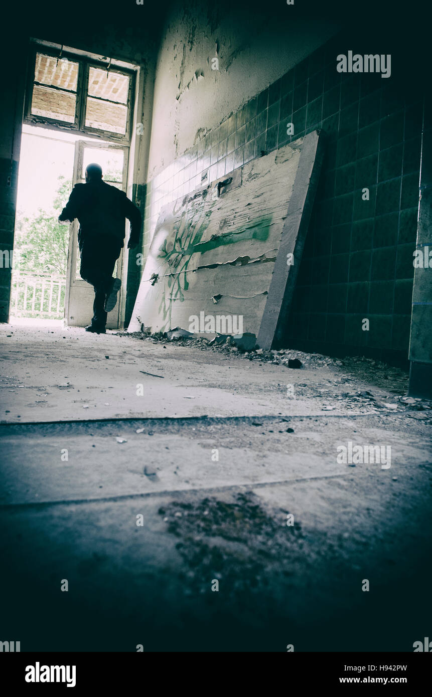 Sinister male figure running out a derelict building Stock Photo - Alamy