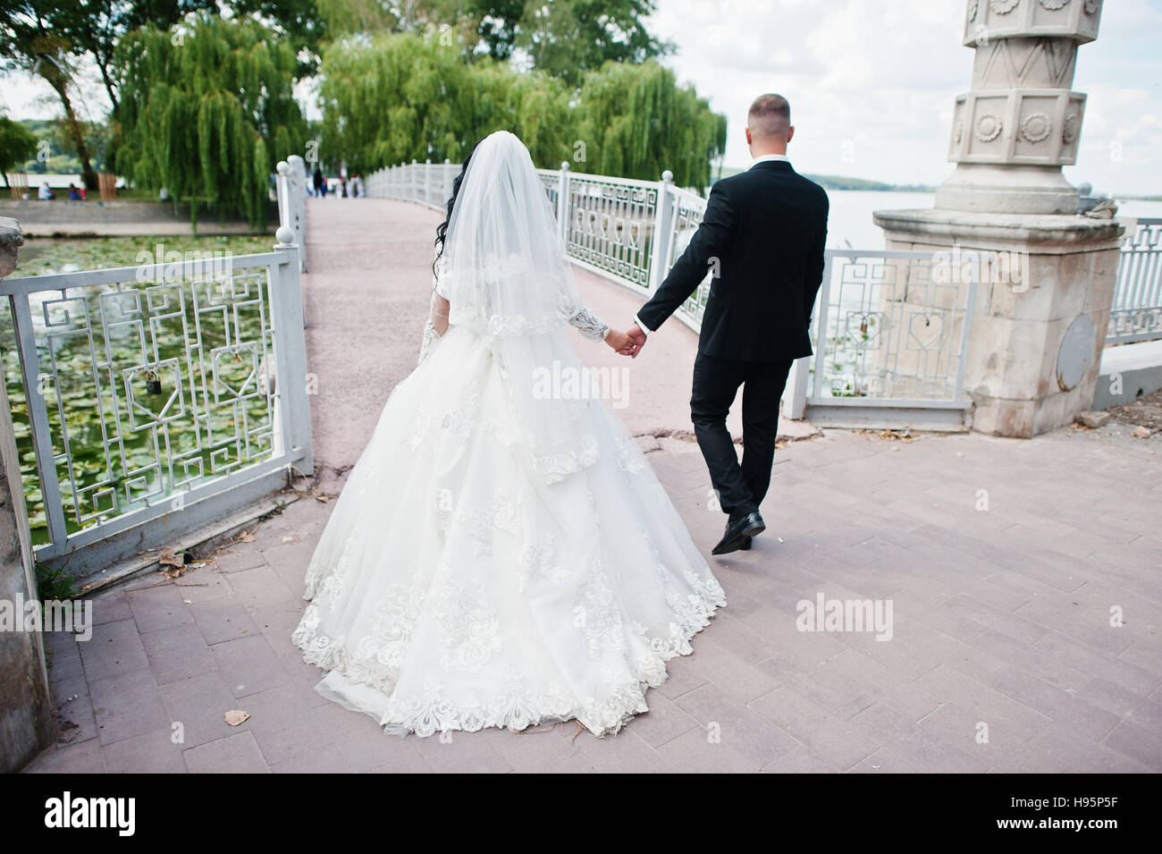 Back view of walking wedding couple at bridge to island of love Stock ...