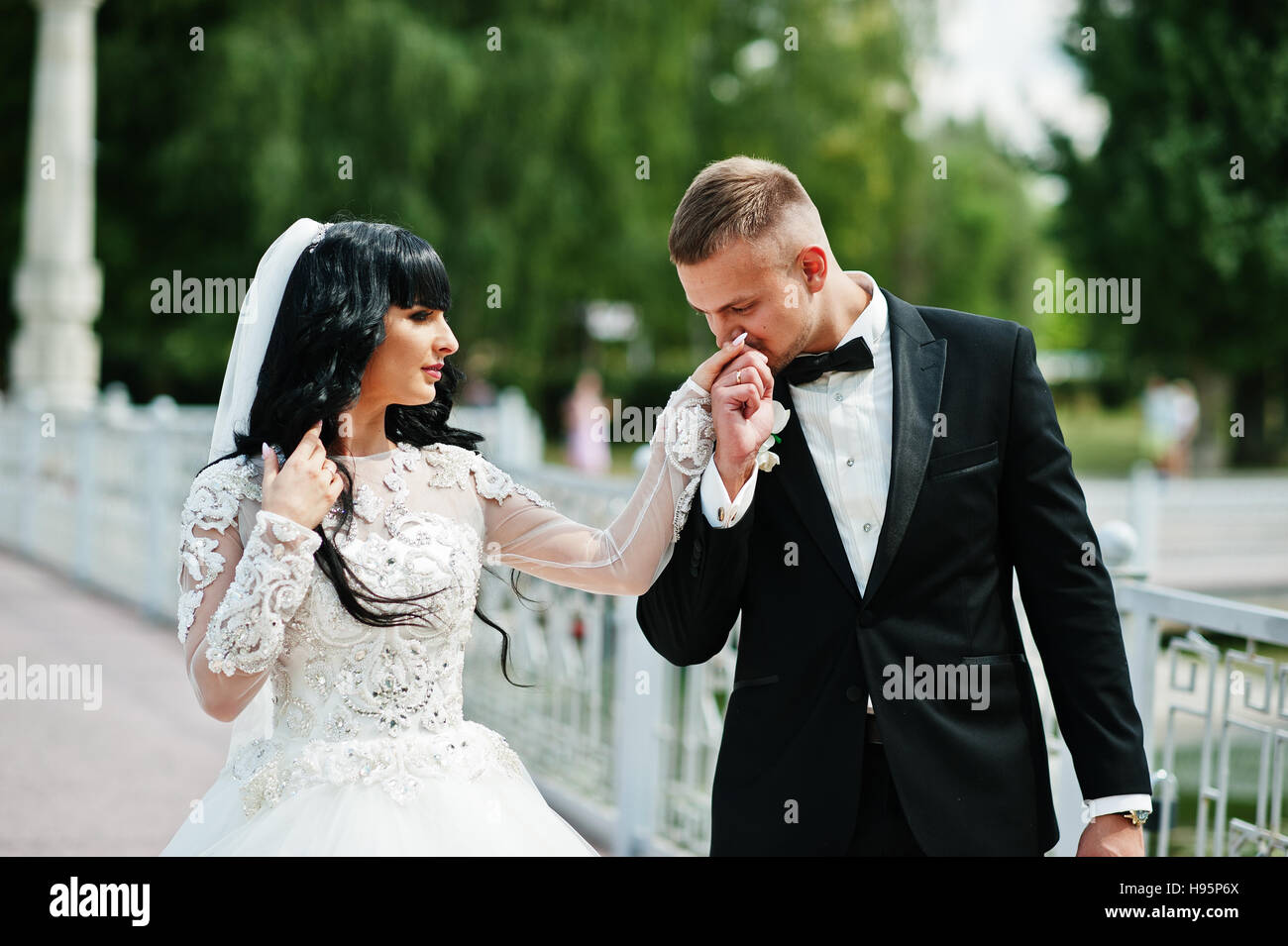 Amazing wedding couple walking on bridge. Groom kiss hand of bride ...
