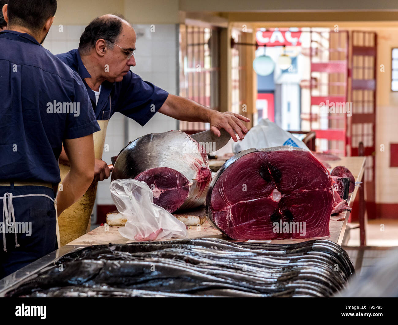 Worker in fish market cutting up a huge tuna fish with a huge knife ...