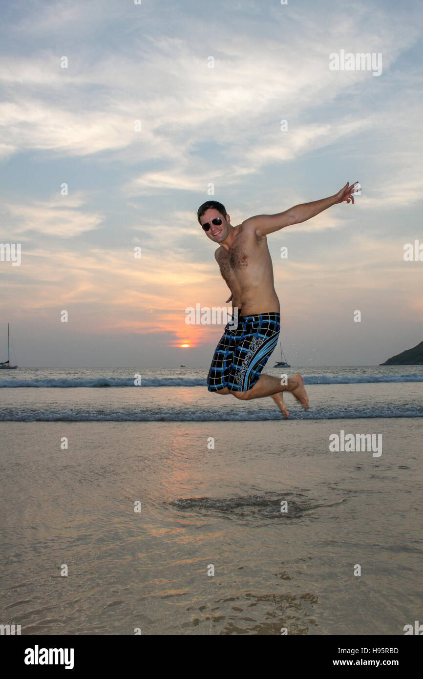 a man jumping happy on the beach with sunset sky in the background ...
