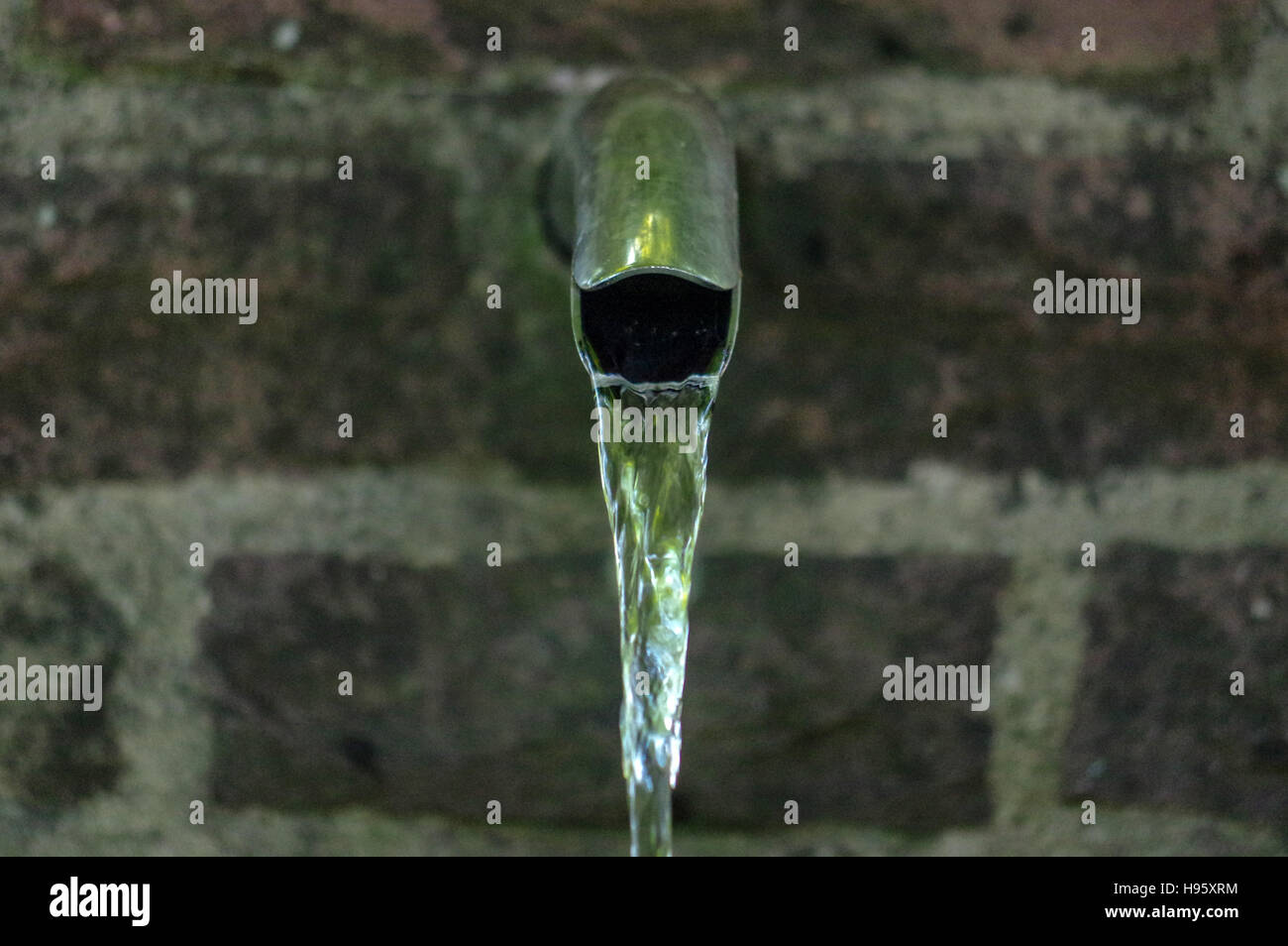 Close up of running water from a tap with brick wall in background ...
