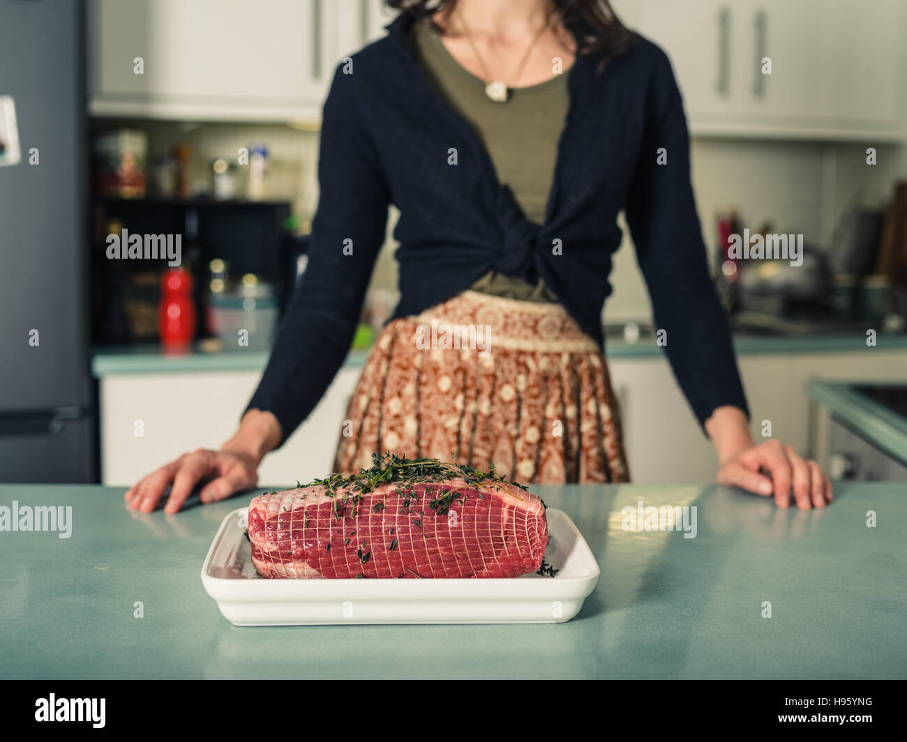 A young woman is standing in a domestic kitchen with a big roasting ...