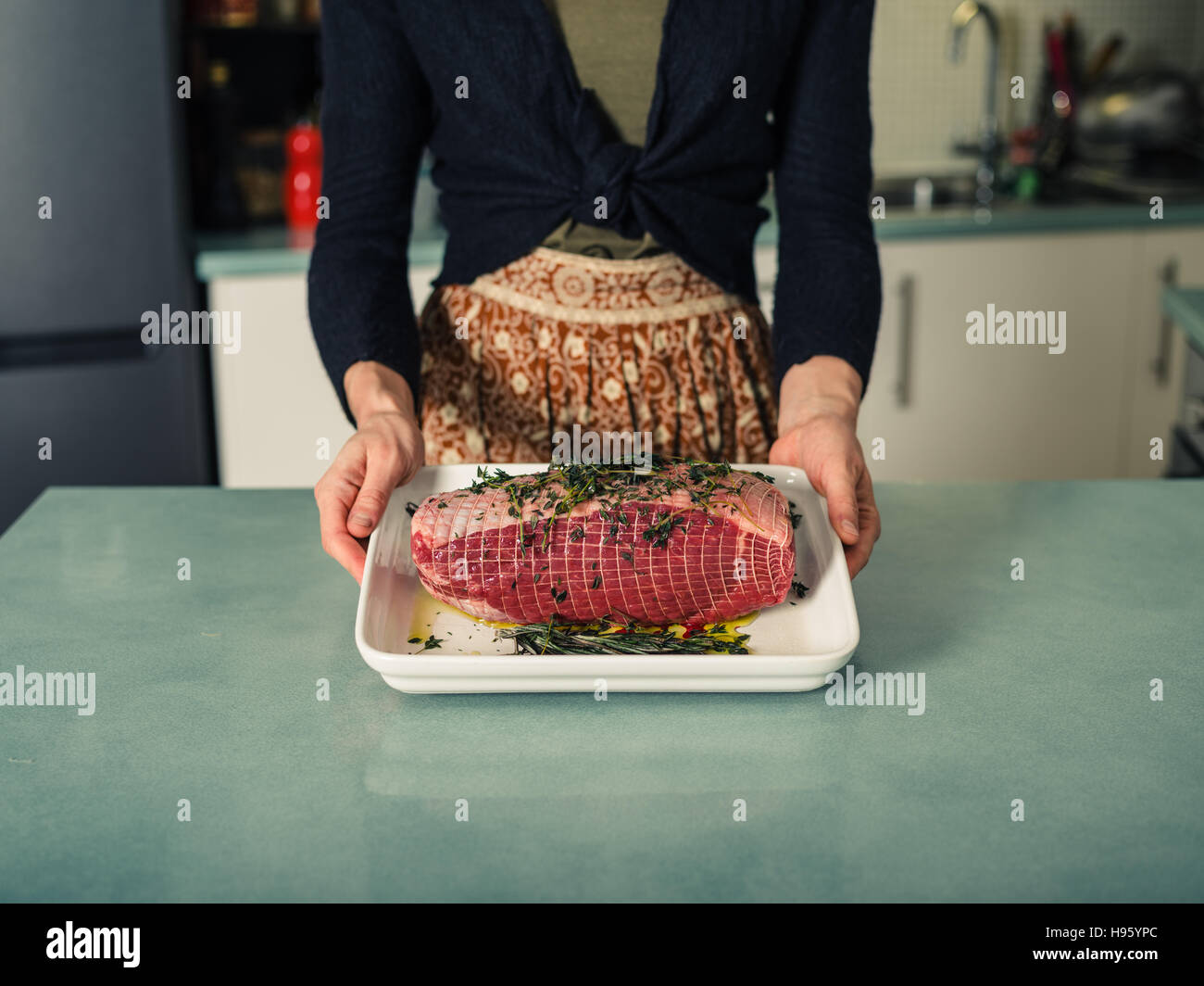 A young woman is standing in a domestic kitchen with a big roasting ...