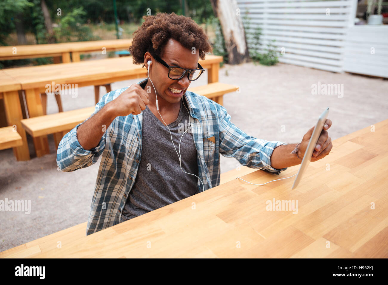 Mad irritated african young man in glasses and earphones using tablet ...