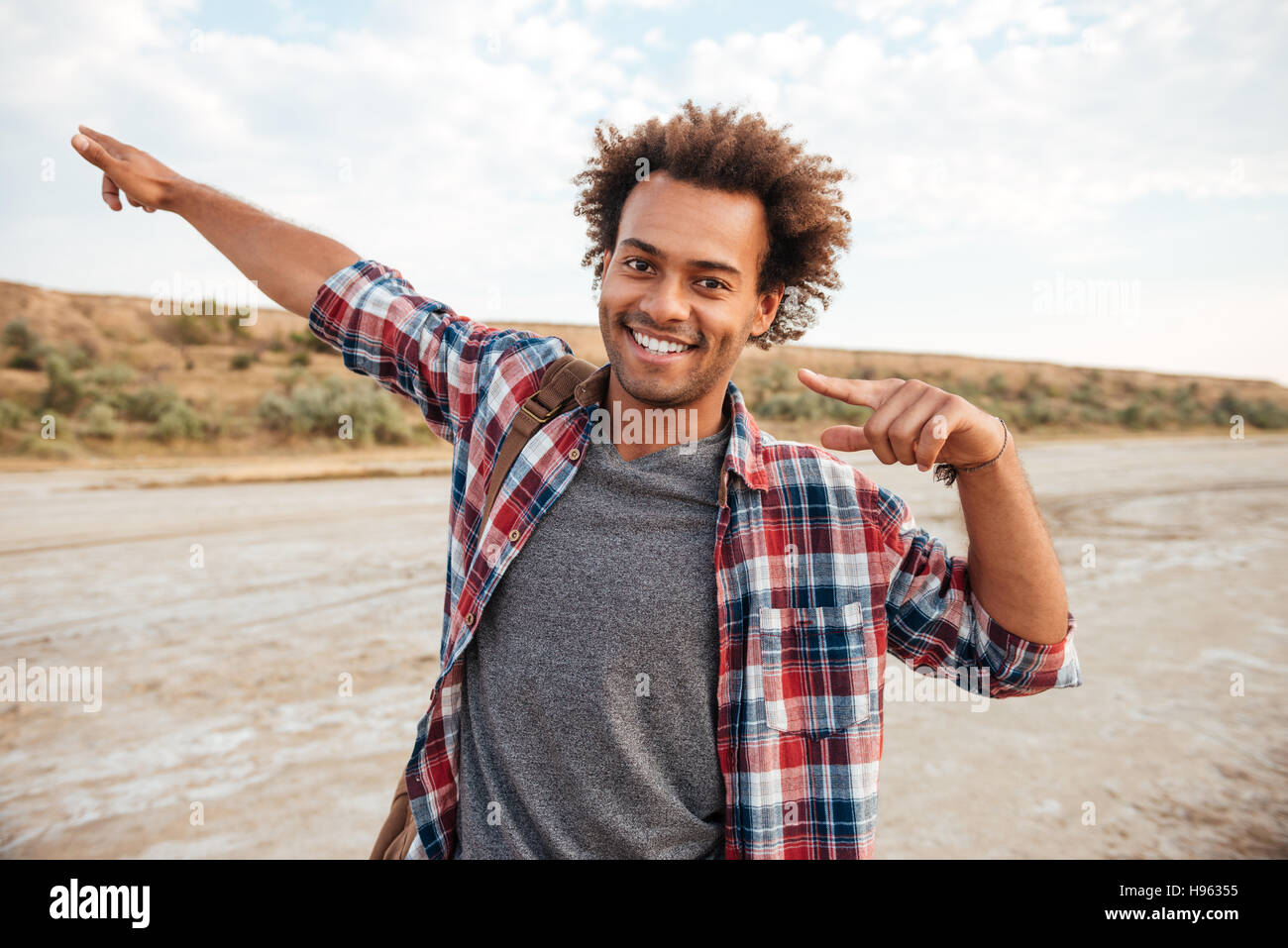 Potrait of smiling african young man with backpack pointing away by ...