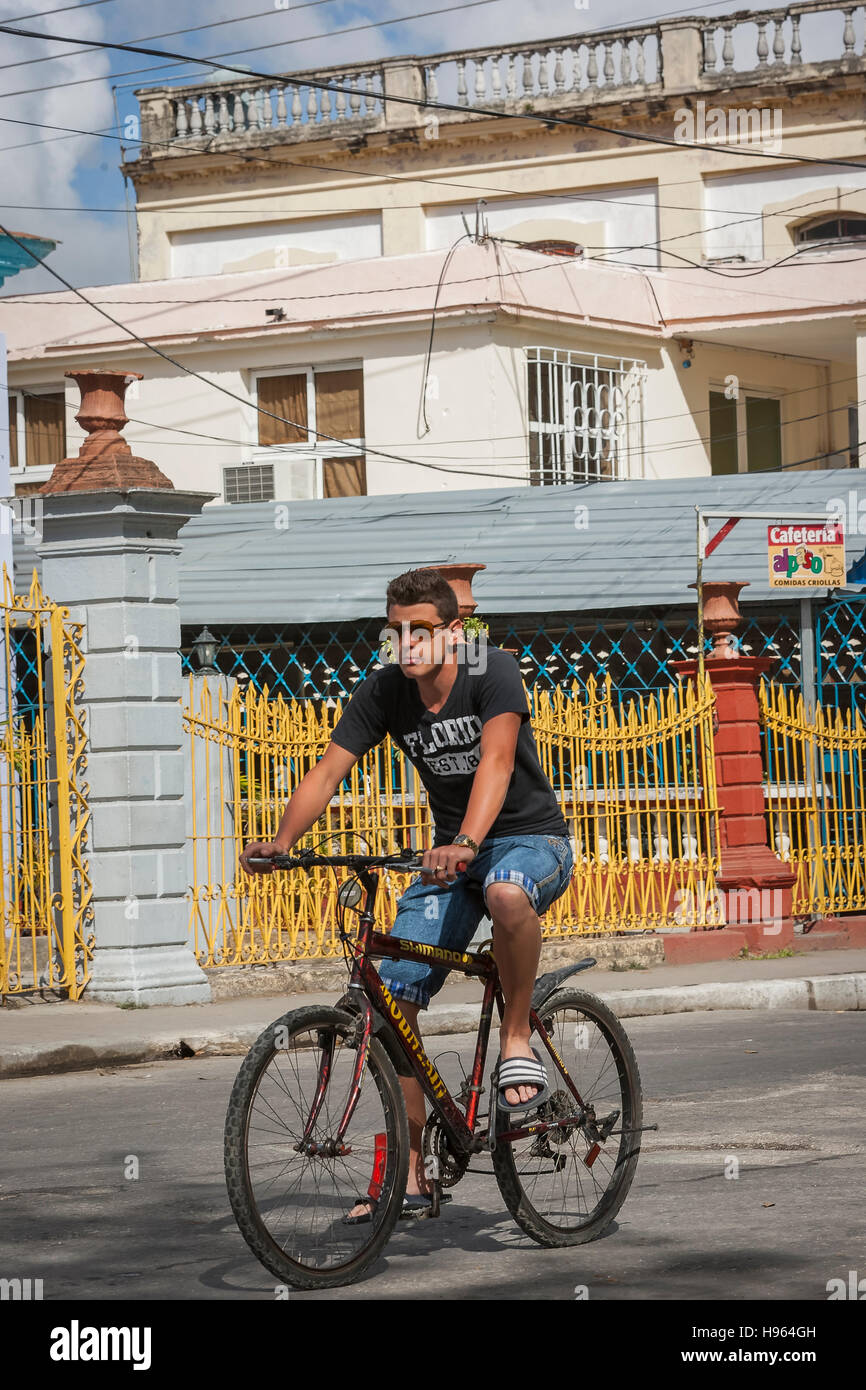Ordinary young man riding a bicycle in a street in Cuba with bright ...