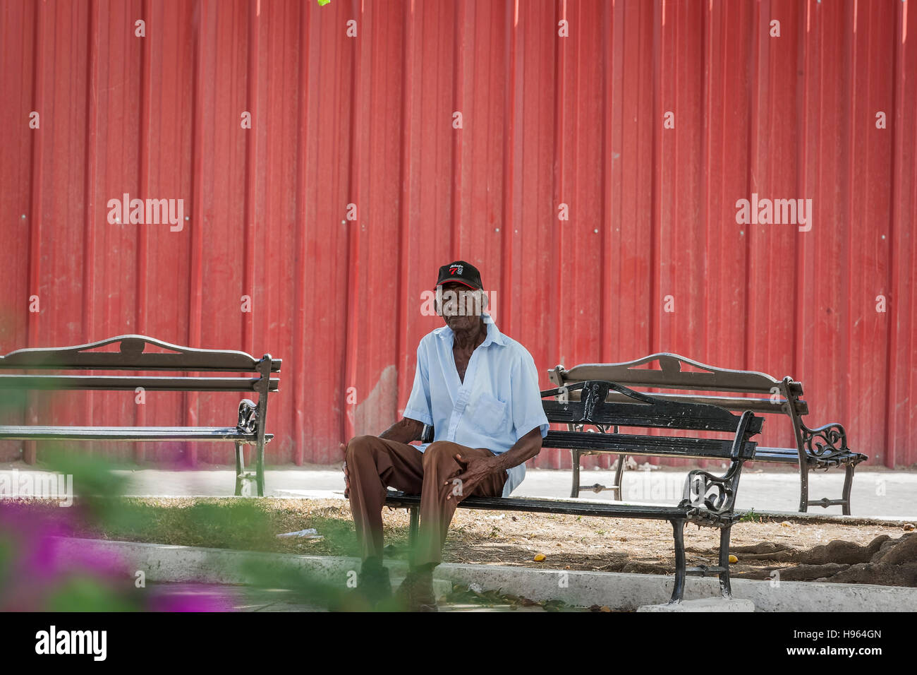 Ordinary old black Cuban man with a cap sitting on a bench with an ...