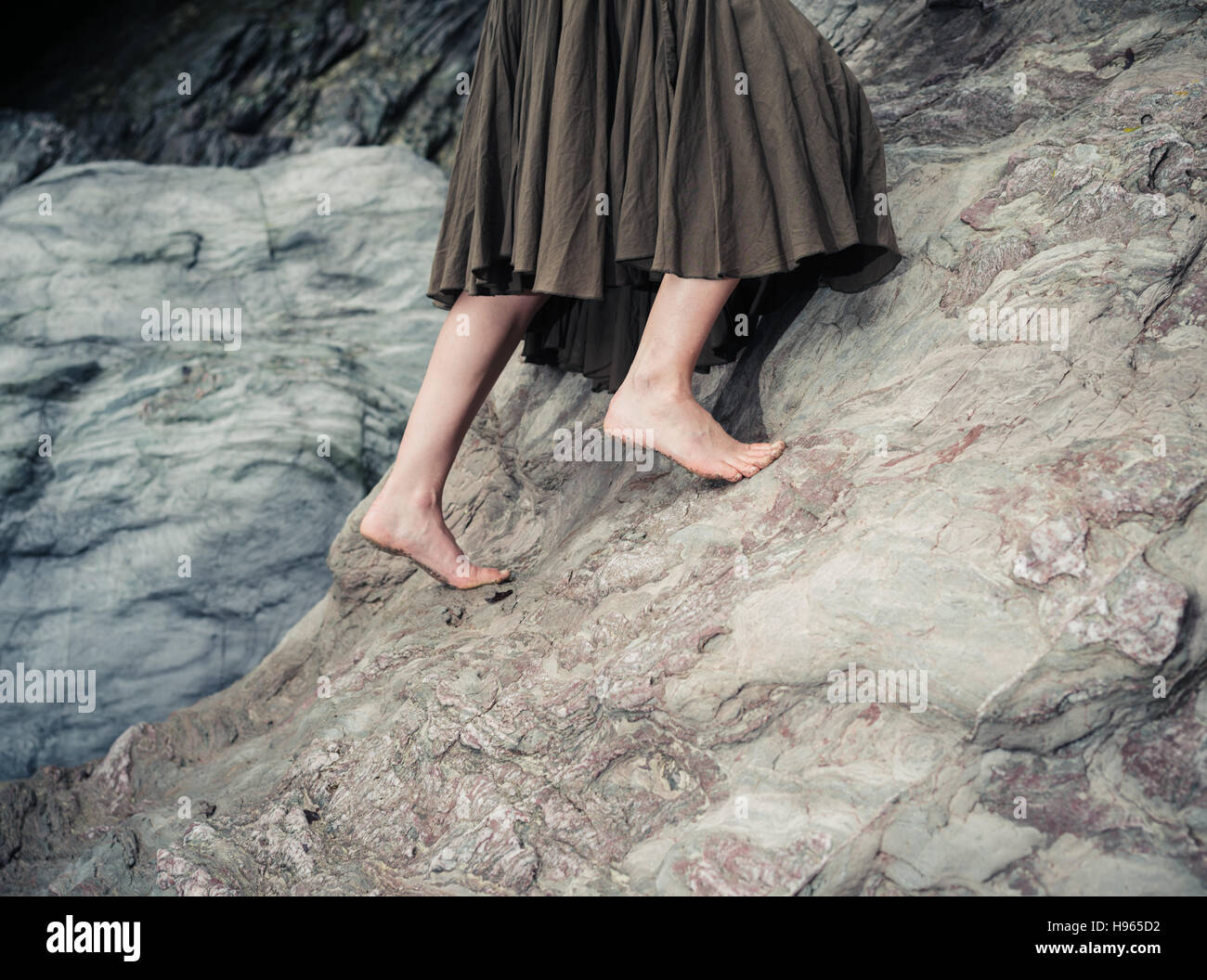 The bare feet of a young woman as she is climbing up a rock surface ...