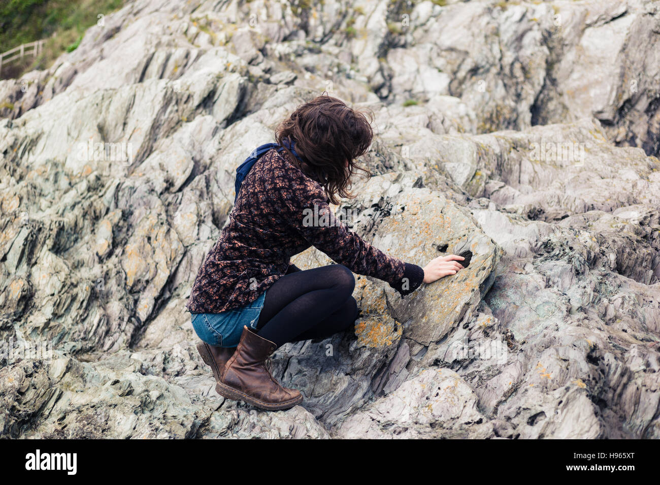 A young woman is sitting on some rocks and is touching a large stone ...