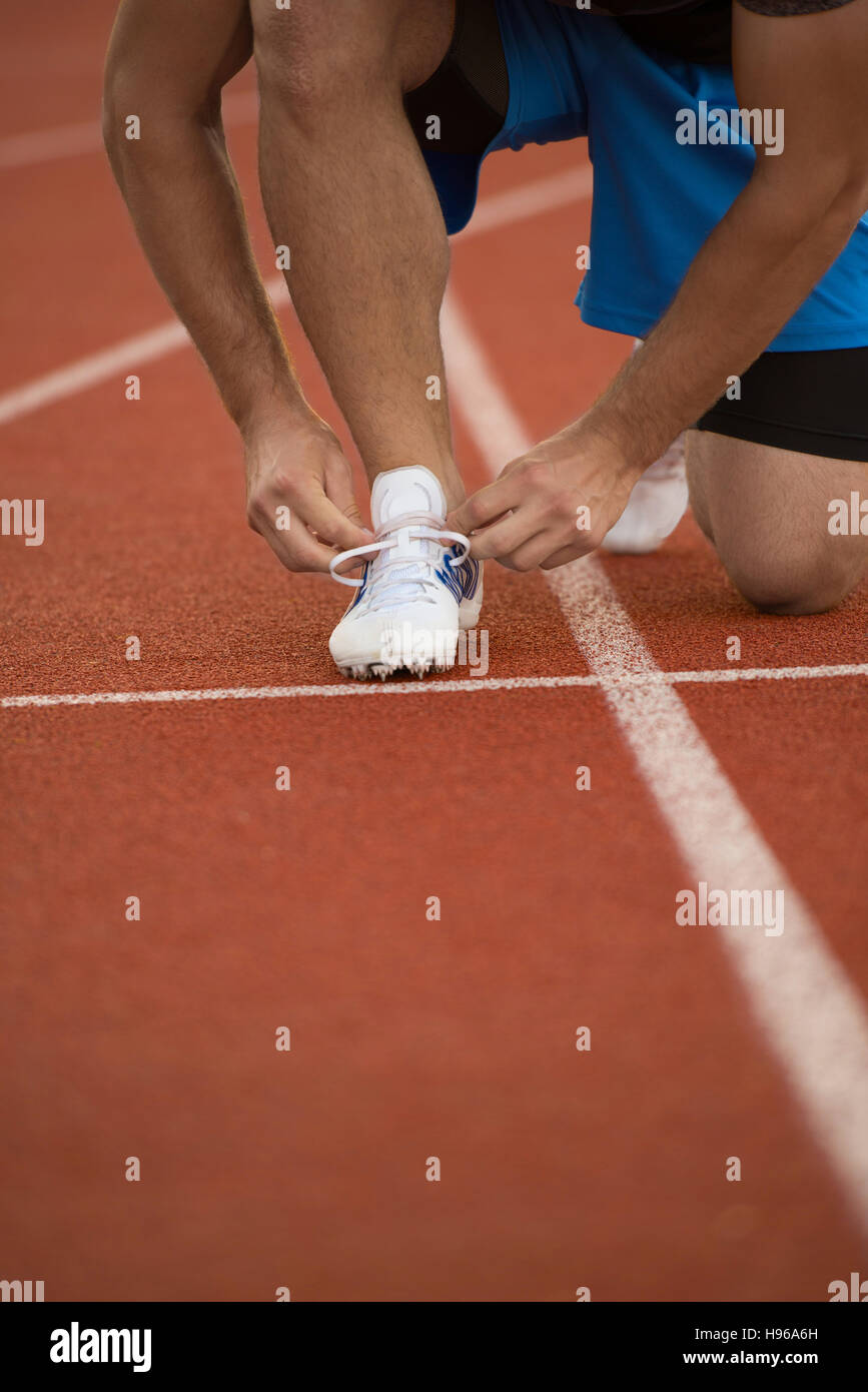 Young Man Runner tying his shoes on a running track. Shoelaces, Urban ...