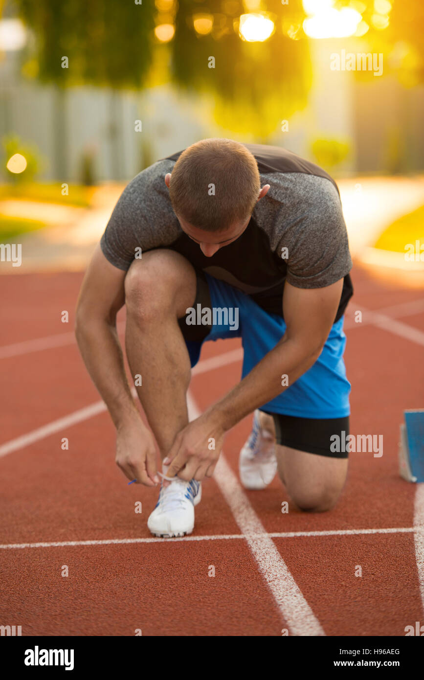 Young Man Runner tying his shoes on a running track. Shoelaces, Urban ...