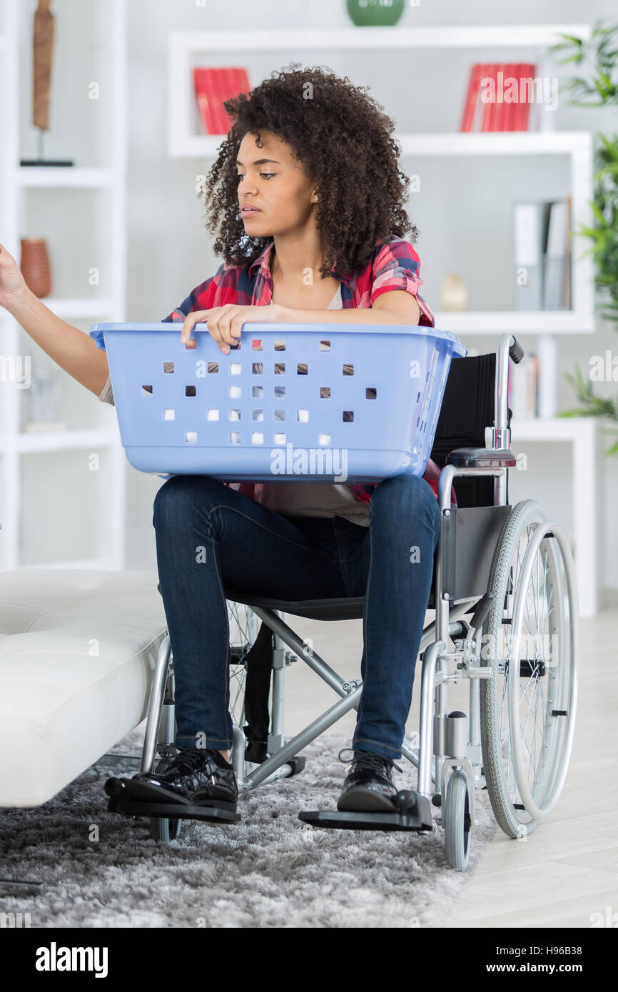 young woman on wheelchair putting laundry into the washing machine ...