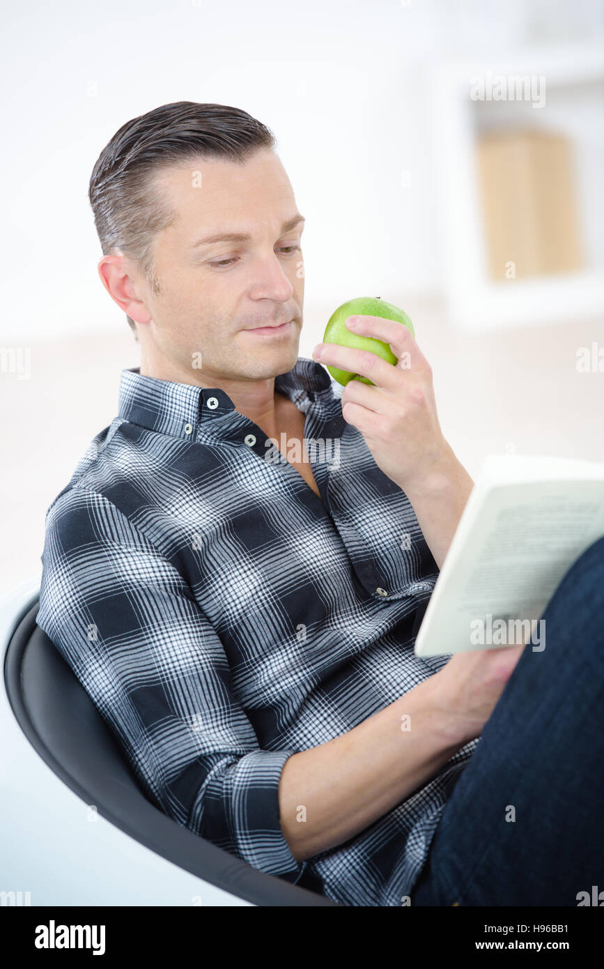 man eating an apple while reading Stock Photo - Alamy