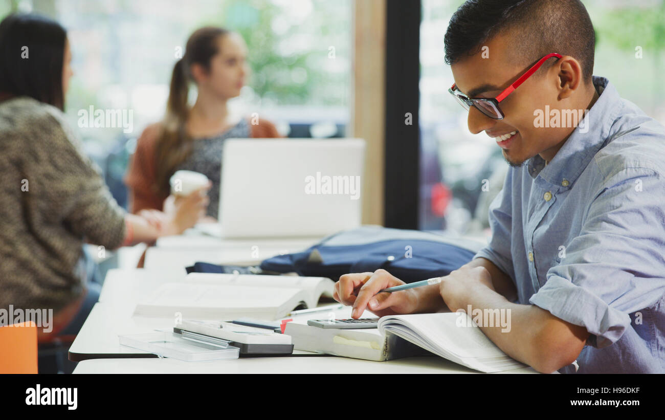 Male college student doing math homework with textbook and calculator ...