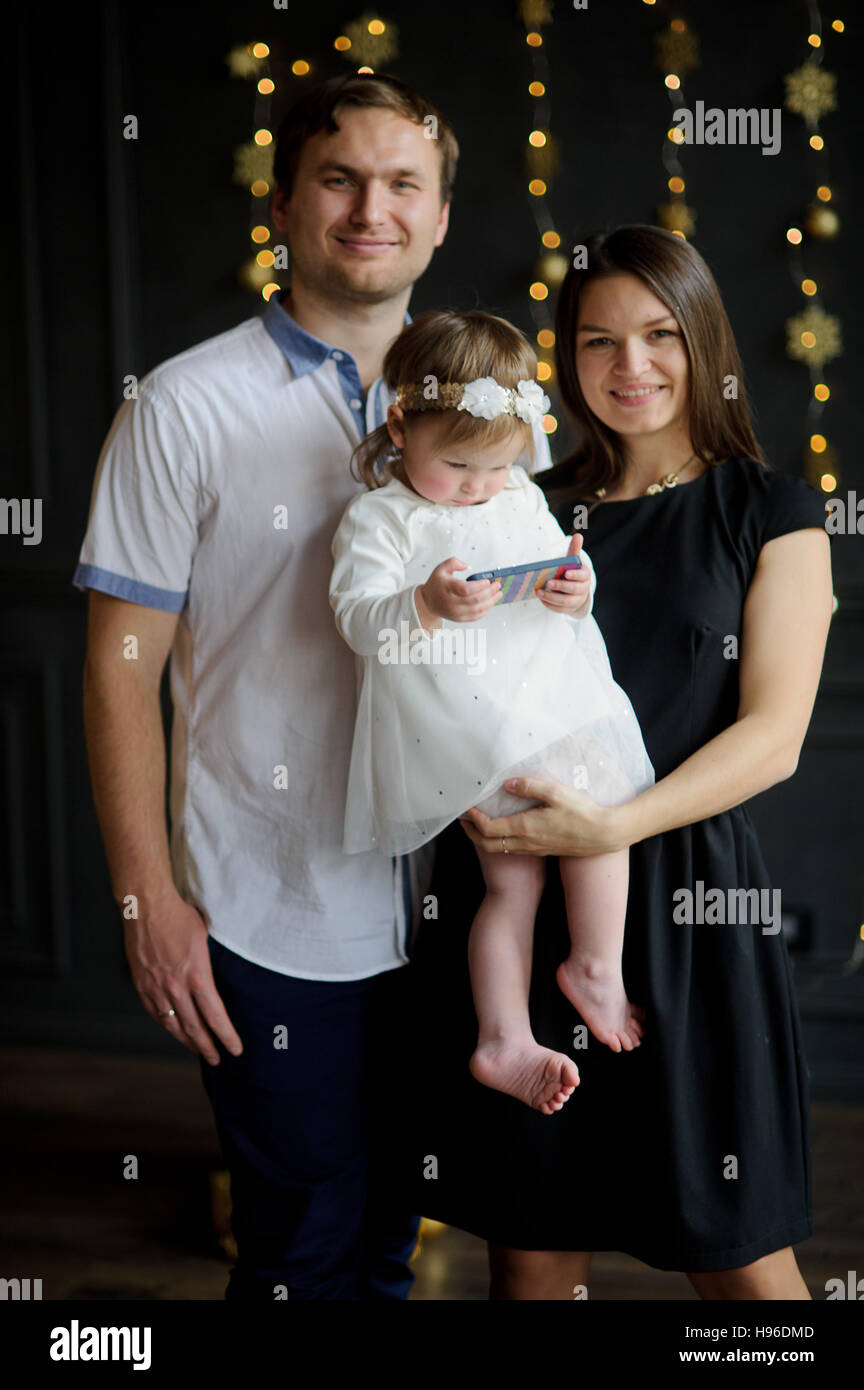 Young family with kid is photographed. Chubby, ruddy girl is elegantly ...