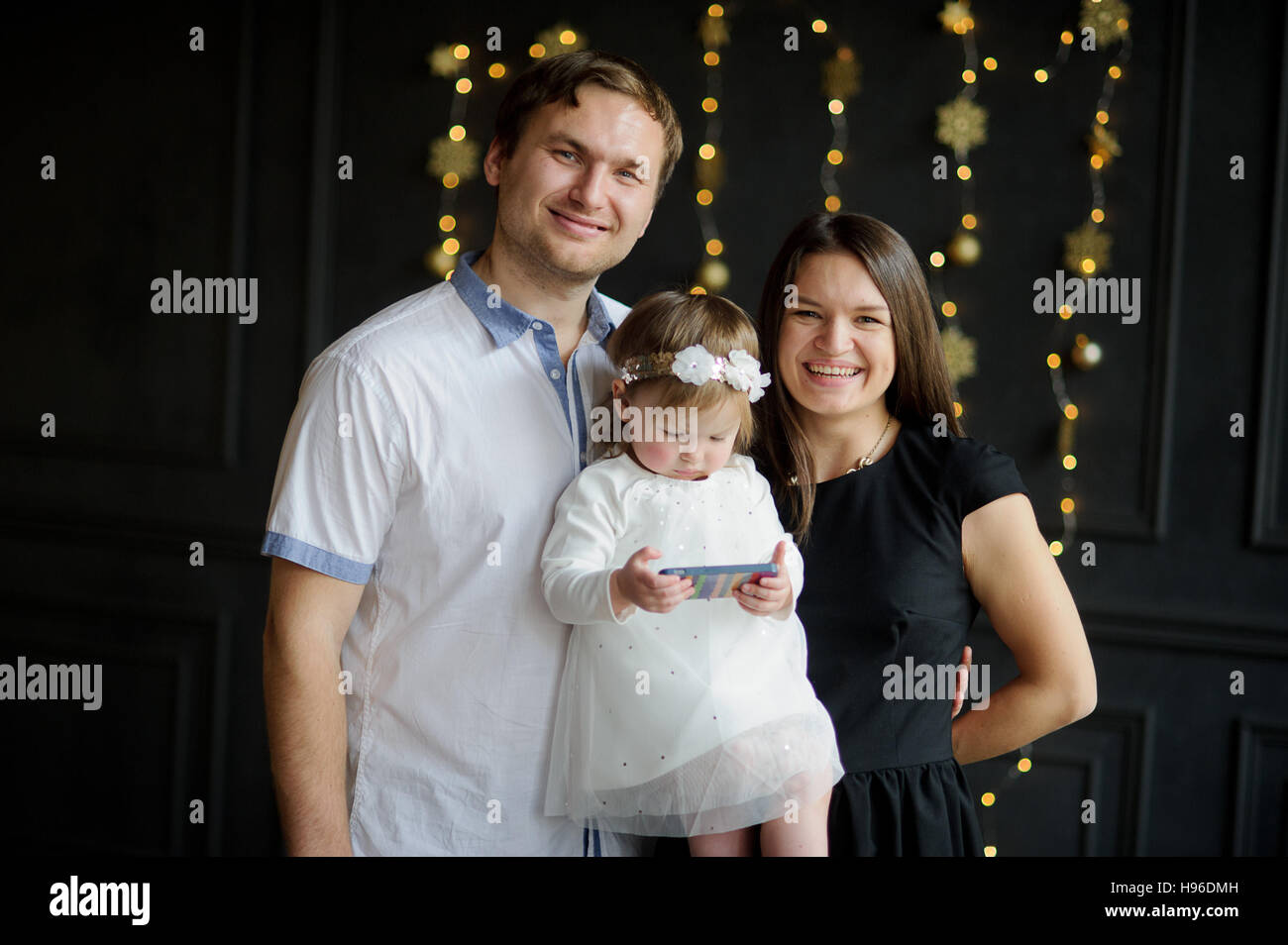 Young family with kid is photographed. Chubby, ruddy girl is elegantly ...