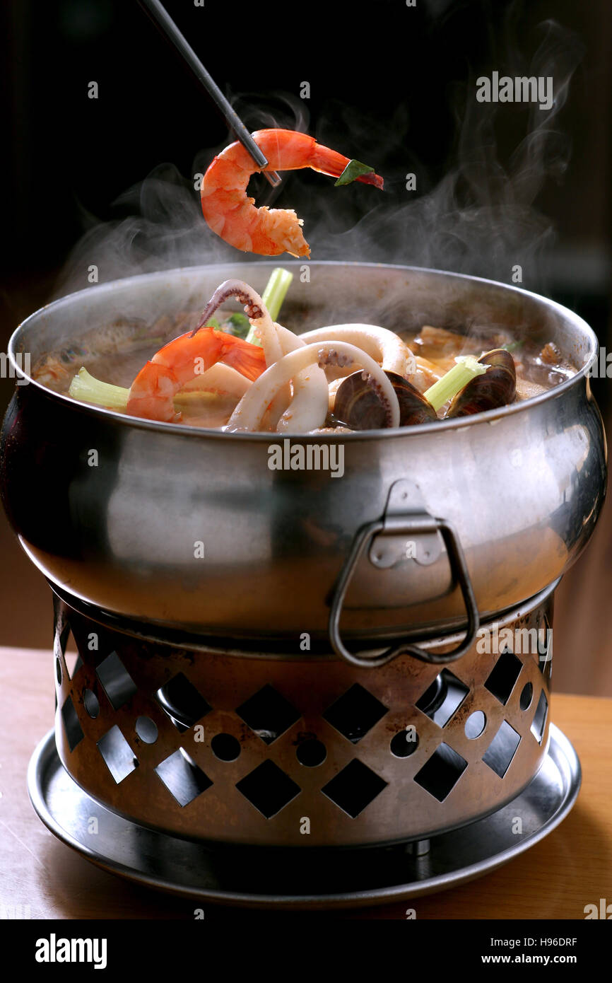 Traditional Chinese seafood hot pot with a shrimp held in a pair of ...