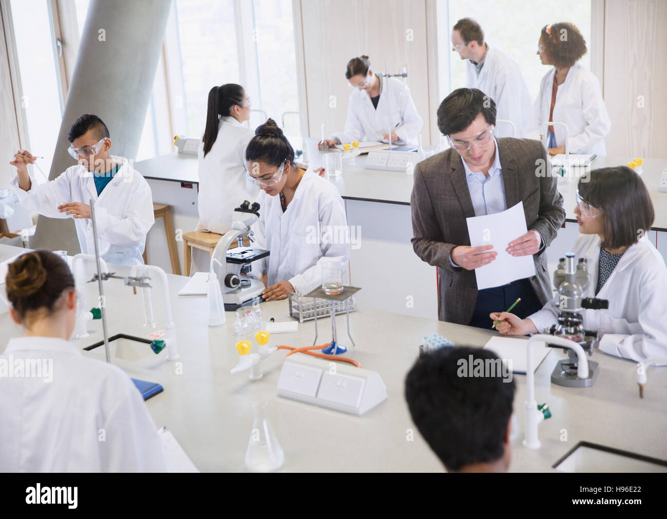 Science professor and college students using microscopes in science ...