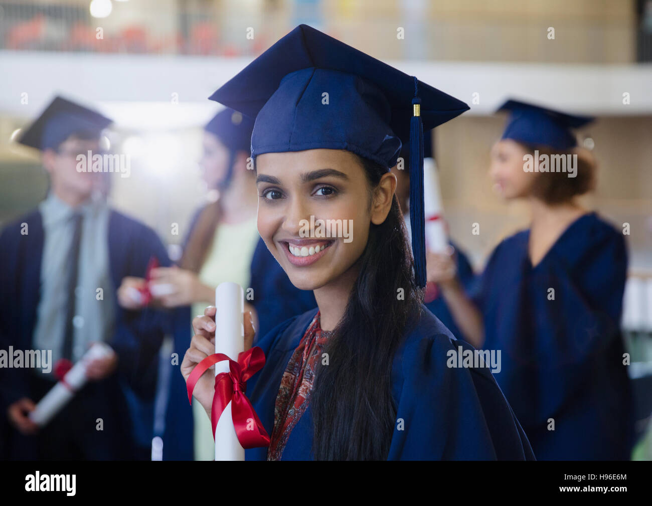 Portrait smiling female college student in cap and gown with diploma ...