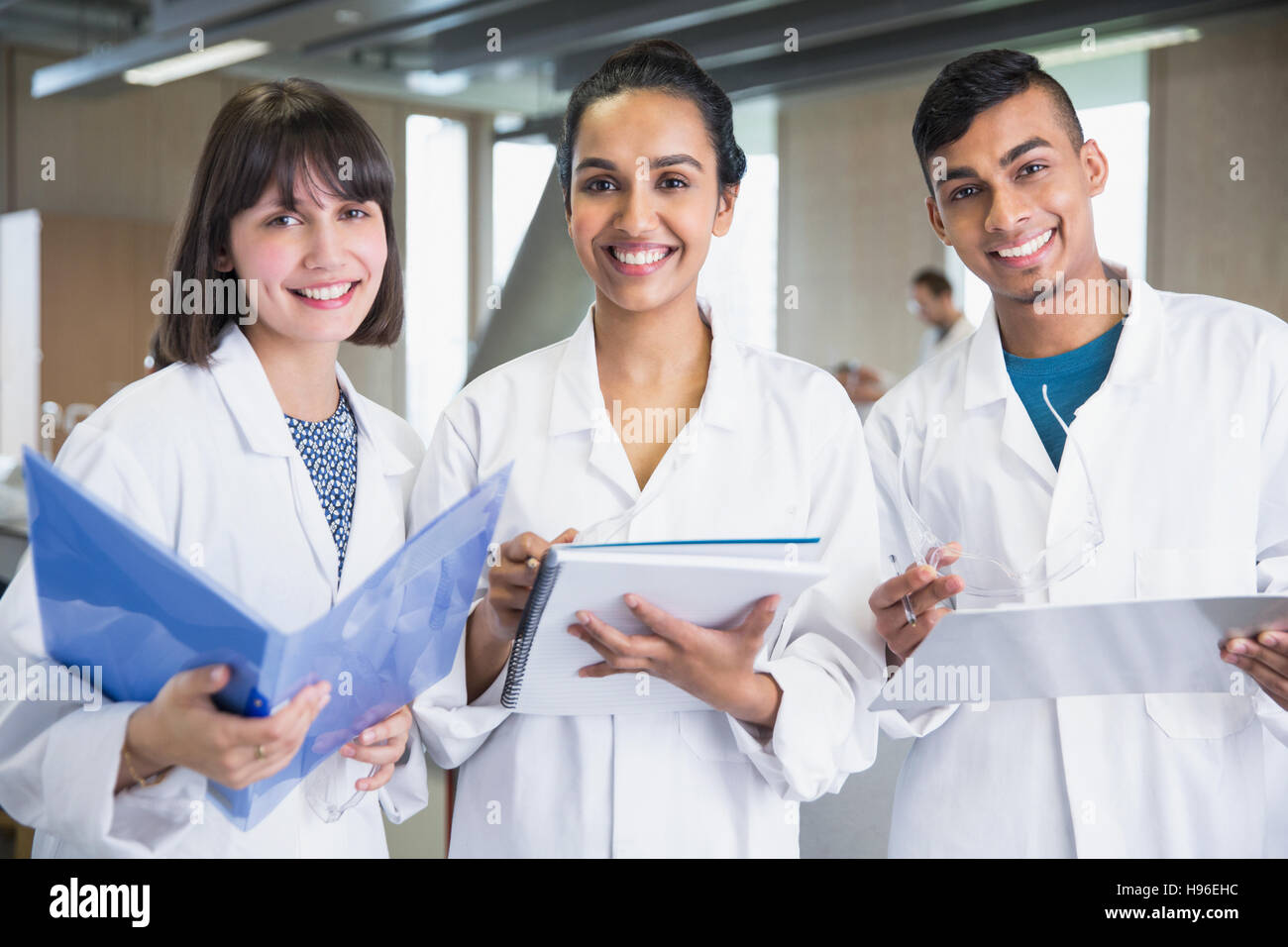 Portrait smiling college students in lab coats with notebooks in ...