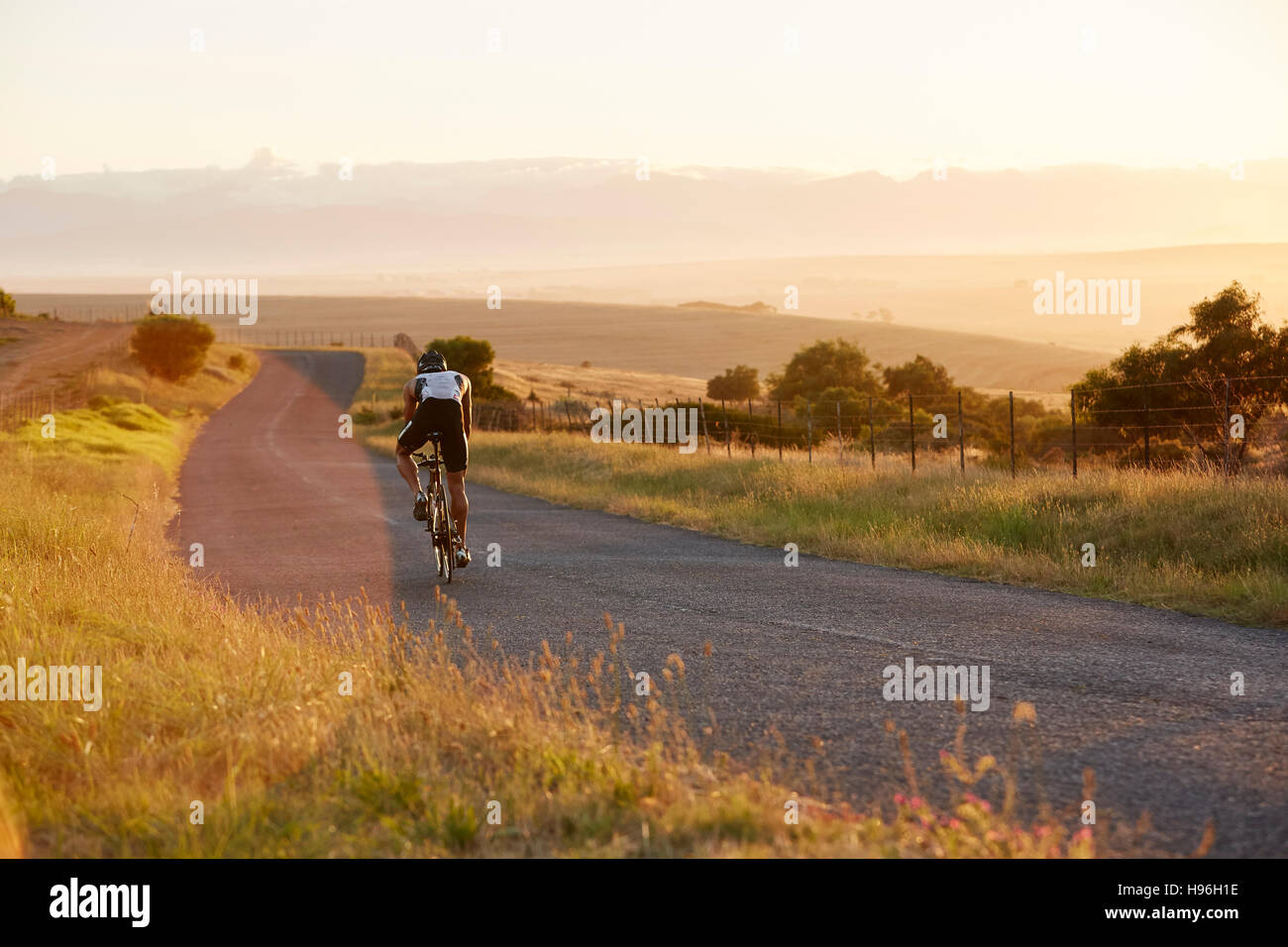 Male triathlete cyclist cycling on sunny rural road at sunrise Stock ...