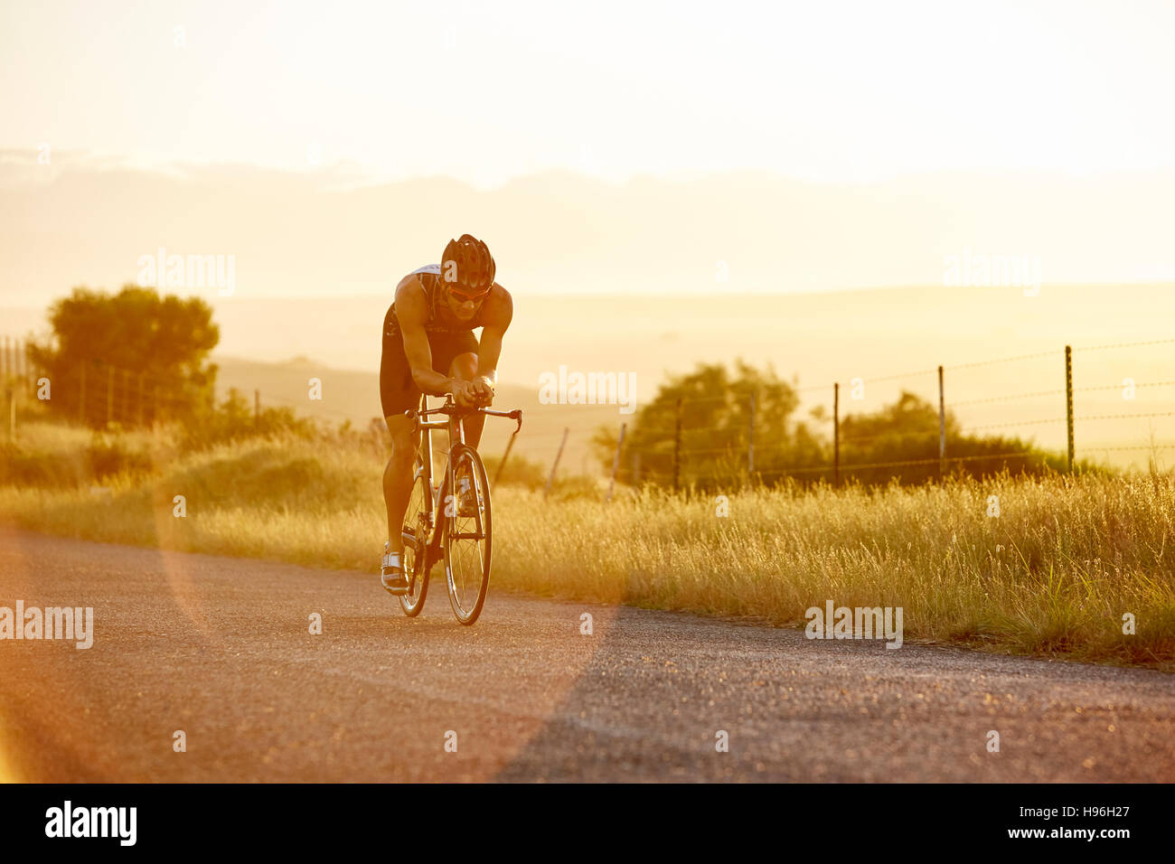 Male triathlete cyclist cycling on sunny rural road at sunrise Stock ...