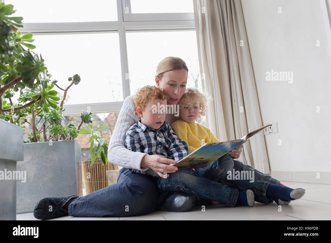 Mother reading to children (4-5, 8-9) in living room Stock Photo - Alamy