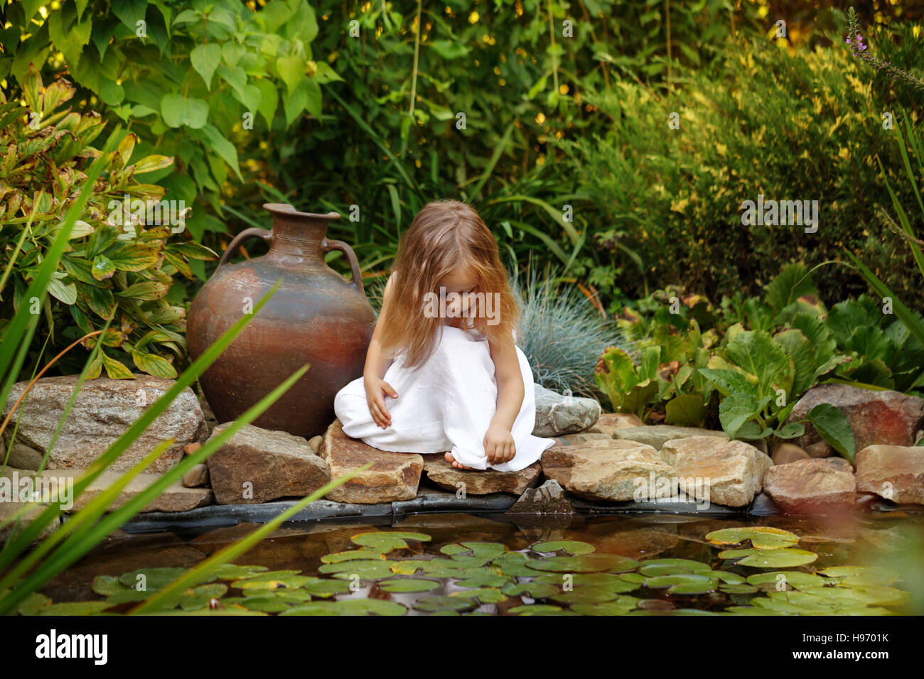 Cute little girl in a white dress looks into the pond with lilies. Big ...
