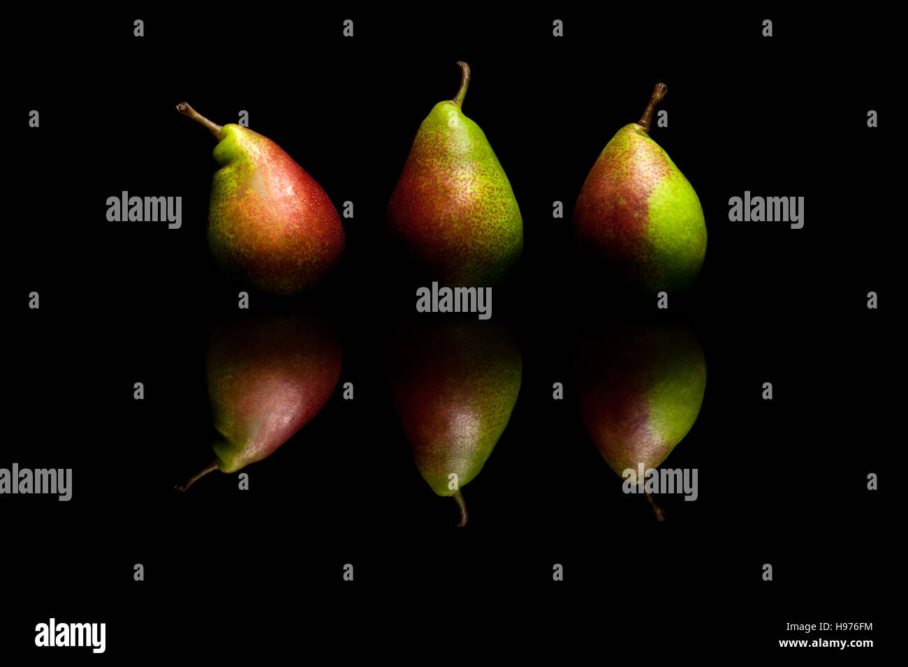 Three whole red and green pears isolated on black reflective background ...